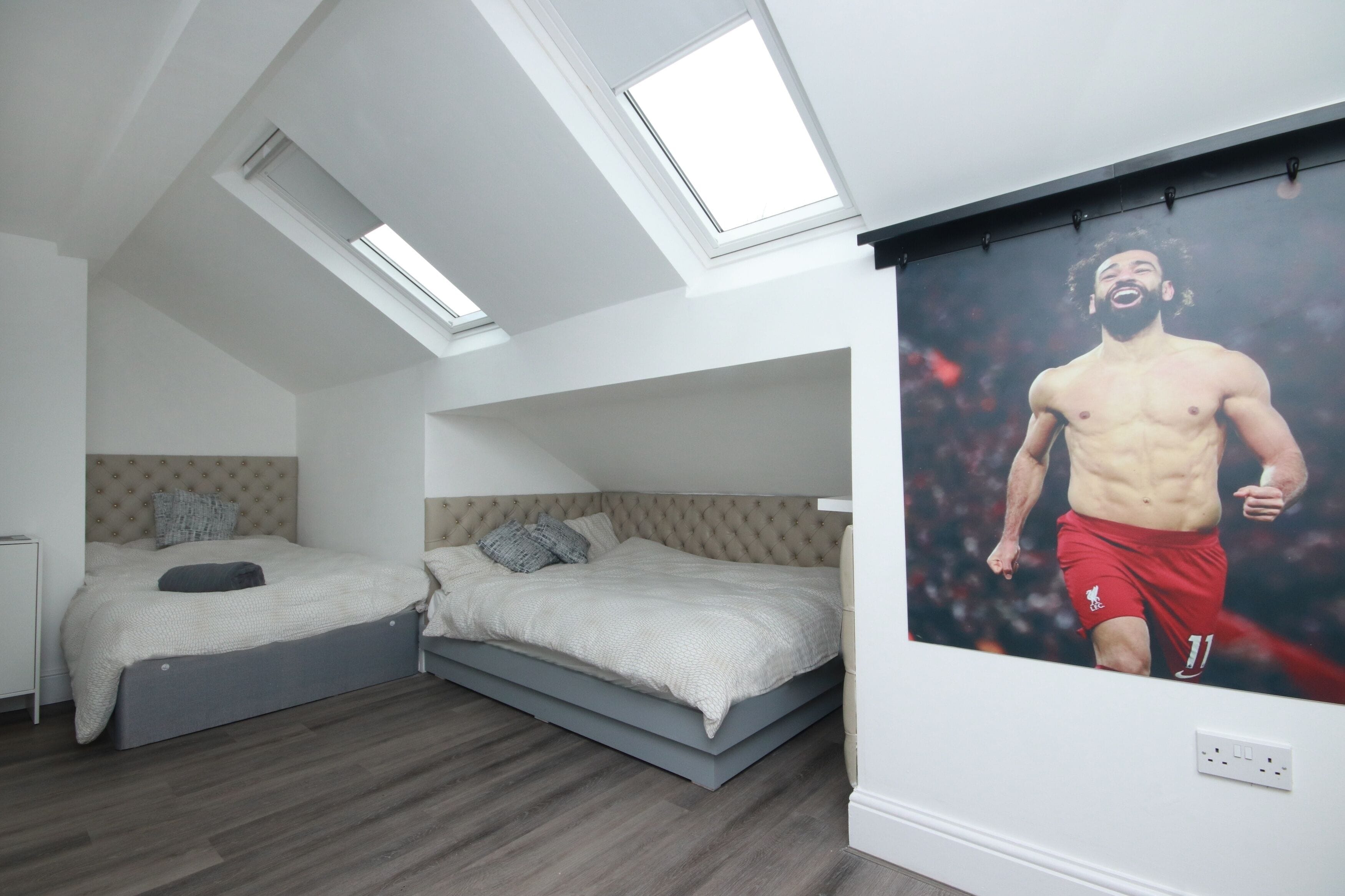 Quarto com cama beliche, claraboias e um pôster grande de um jogador de futebol.