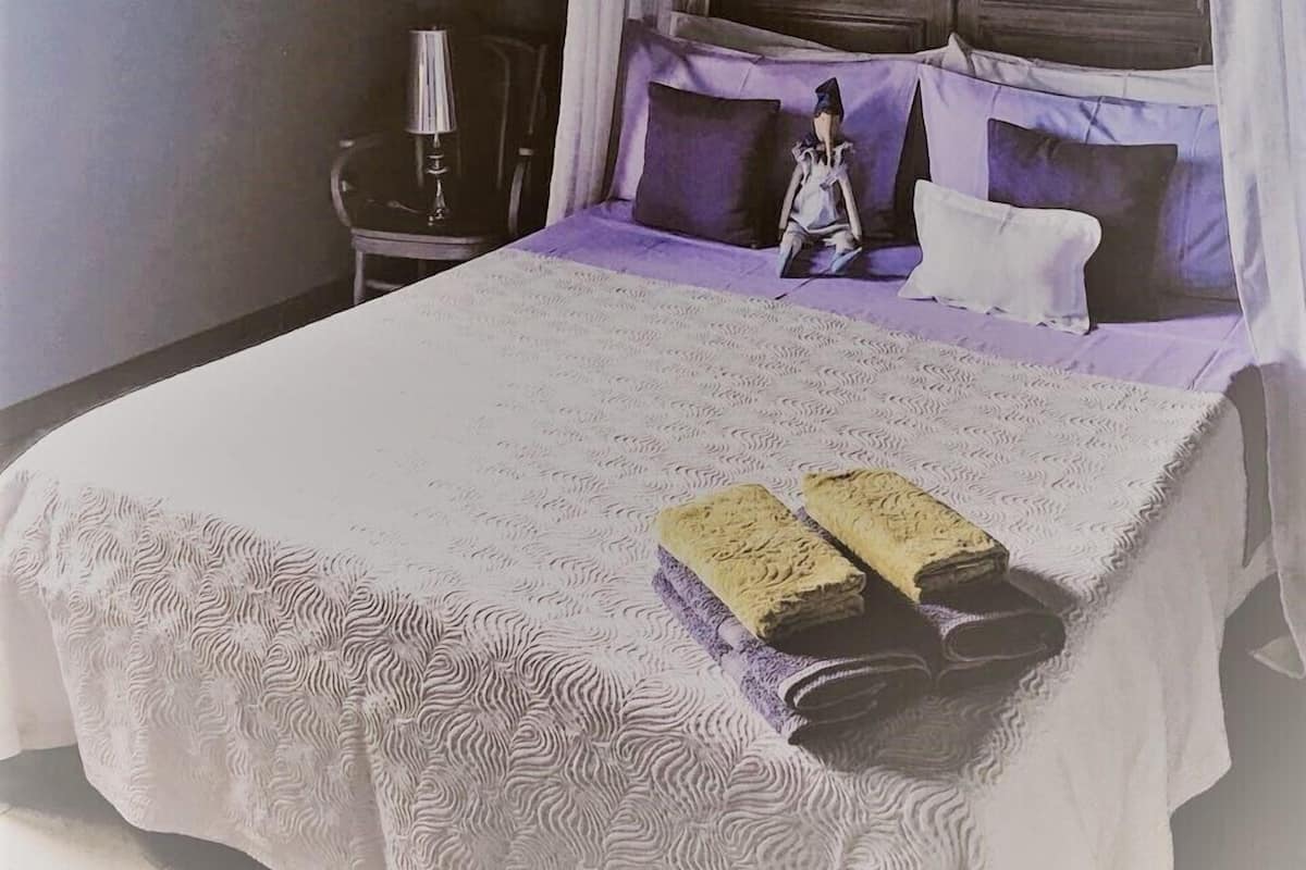 Quarto com cama grande, cabeceira decorativa, mesa de cabeceira e luminária suspensa.