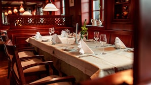 Restaurante com uma mesa comprida posta para refeição, cadeiras de madeira e luminárias pendentes.