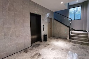 Um elevador moderno, uma escadaria e uma lixeira em uma área de hall.