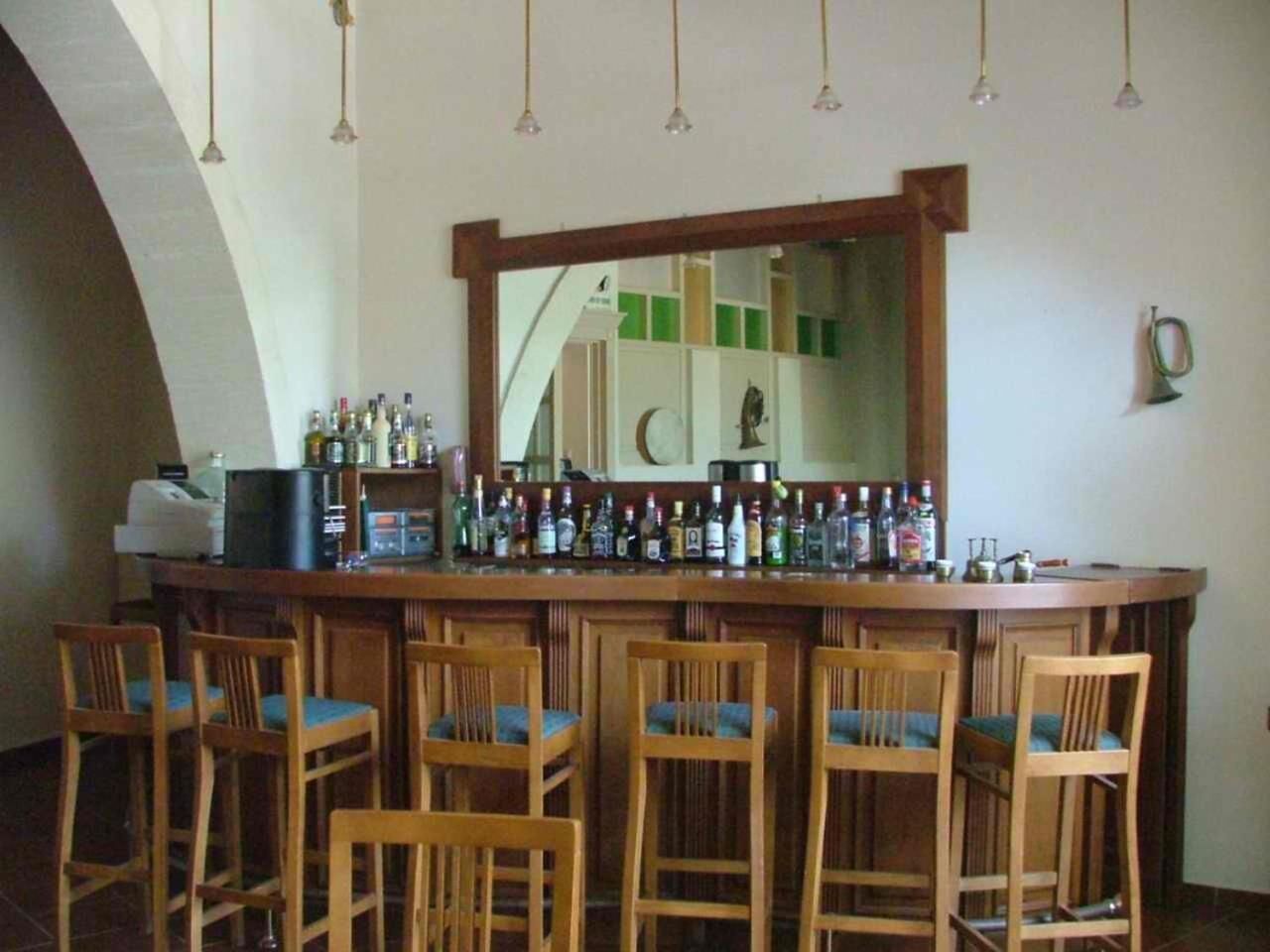 Uma área de bar com cadeiras de madeira, um balcão com diversos frascos e um espelho grande.