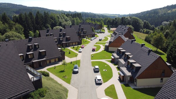 Uma área residencial com várias casas, uma rua central e vegetação ao redor.