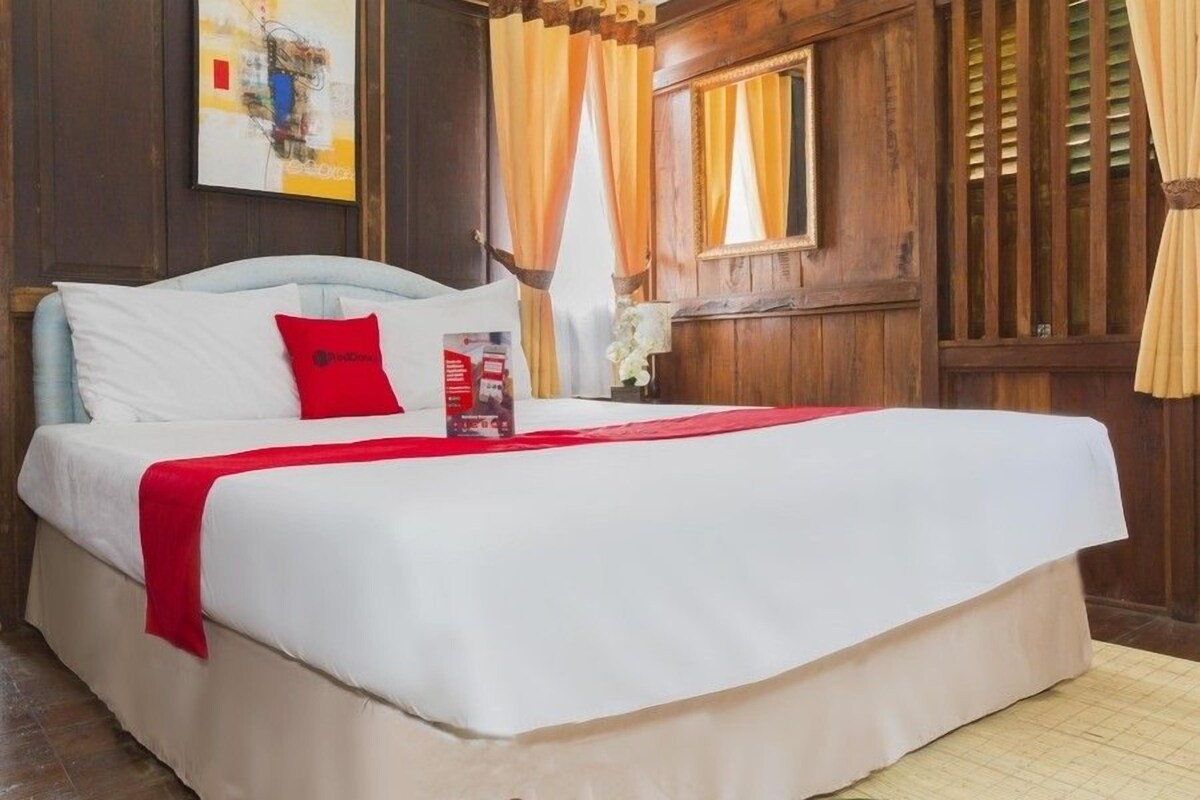 Cama com roupa de cama branca, um travesseiro e um cobertor vermelhos. Há uma moldura com uma fotografia na parede acima da cama.
