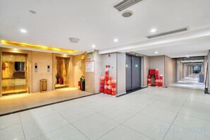 Um hall de hotel com balcão de recepção, área de espera e corredor que dá acesso a elevadores.