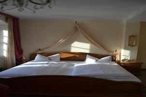 Uma cama de casal com cabeceira de madeira, mesa de cabeceira com abajur e janela com cortinas.