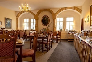 Uma área de jantar com mesas e cadeiras de madeira, um candelabro e um retrato na parede.