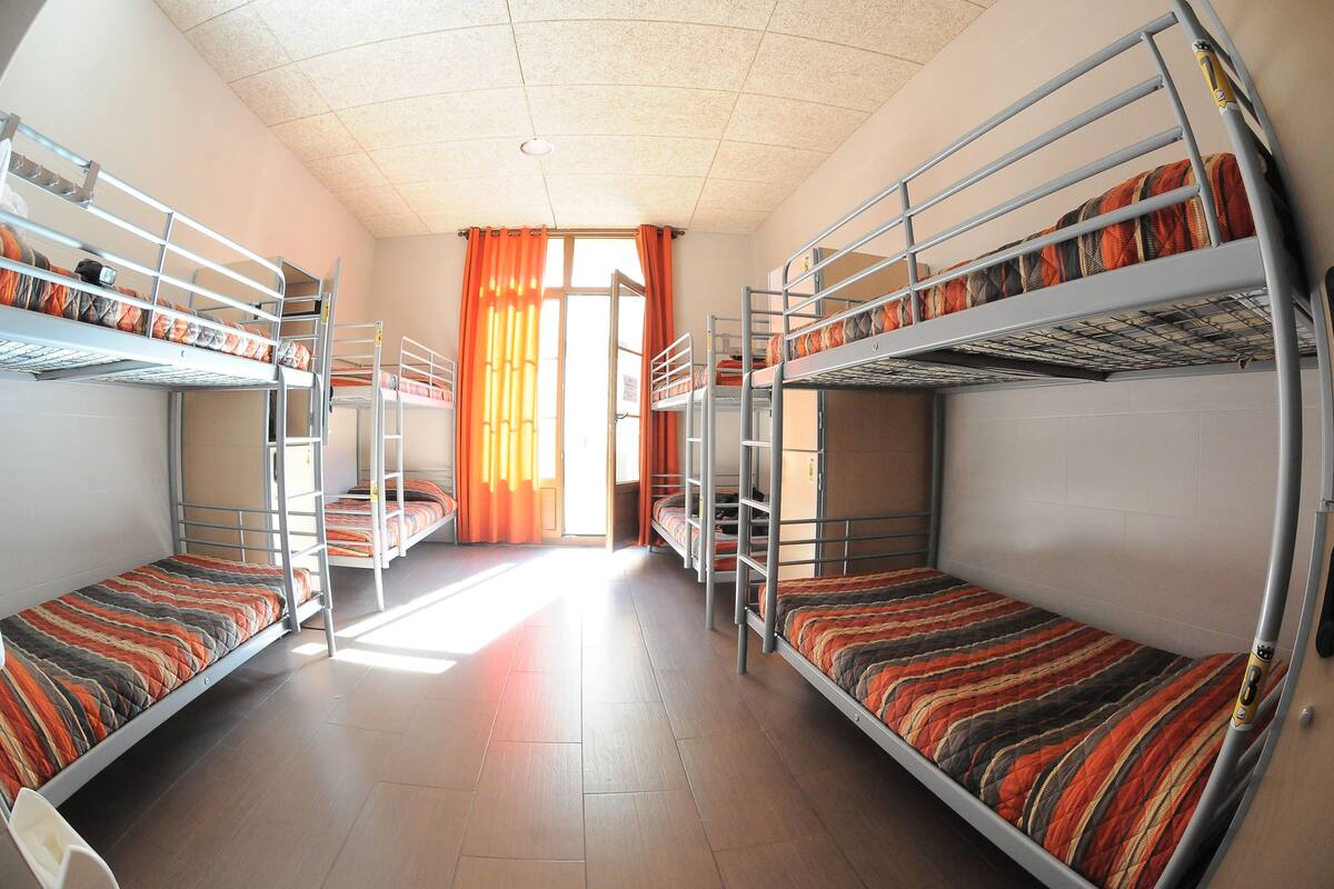Um quarto em dormitório com beliches, piso de azulejos e uma janela com cortinas laranja.