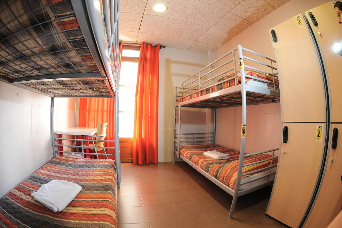Quarto de dormitório com beliches, uma escrivaninha e um frigorífico.