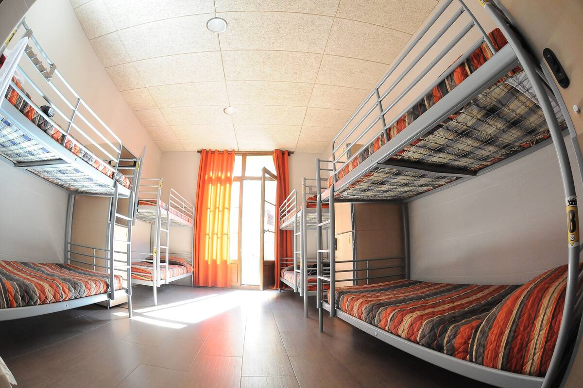 Um dormitório com beliches, uma janela com cortinas laranja e teto de azulejos.