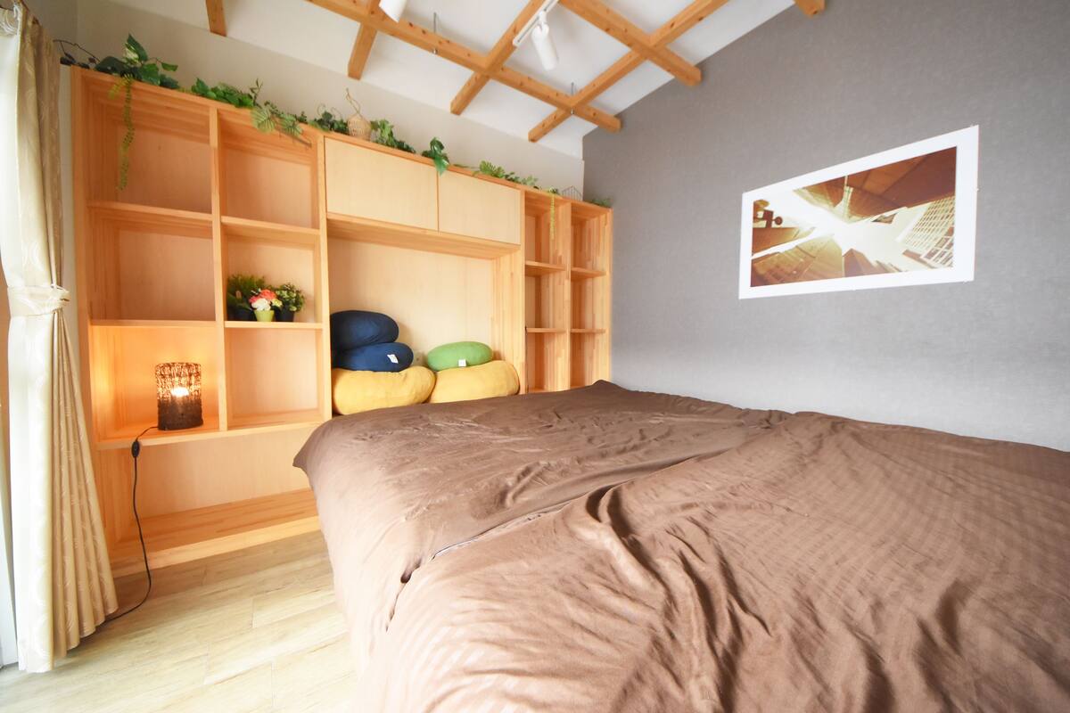 Quarto com cama, estante de madeira com plantas e quadro na parede.