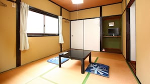 Um quarto japonês tradicional com tatames, uma mesa baixa, uma televisão e portas deslizantes.