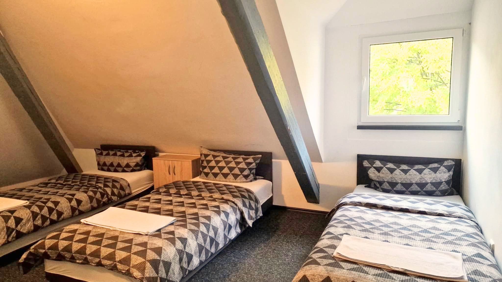 Quarto com duas camas, cada uma com roupa de cama estampada, um armário de madeira e janela com vista para o verde.