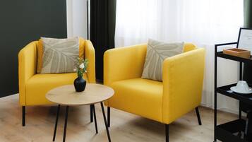 Um quarto com duas poltronas amarelas, uma mesa redonda pequena e uma mesinha lateral de metal preto com uma chaleira branca.