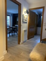 Um corredor com piso de madeira, uma área de jantar com cadeiras e uma mesa, e um quadro na parede.