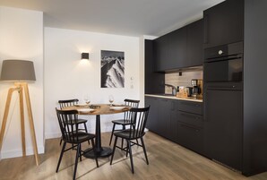 Uma cozinha moderna com armários pretos, uma mesa de jantar de madeira com quatro cadeiras e uma grande fotografia em preto e branco na parede.