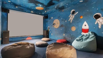 Quarto com mural com tema espacial, poltronas de feijão e tela de projetor.