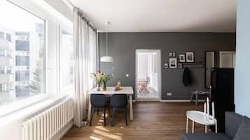 Uma sala de estar moderna com um sofá cinzento, um espaço de jantar com mesa e cadeiras, e uma janela grande com cortinas.