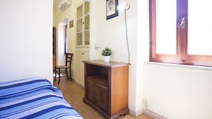 Quarto com cama, mesa de cabeceira de madeira, cadeira, janela e porta de acesso a um banheiro.