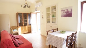 Uma sala de jantar com uma mesa posta para quatro pessoas, um sofá vermelho e uma cadeira de vime.