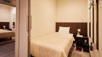 Quarto de hotel com cama, mesa de cabeceira, espelho e sapateira.