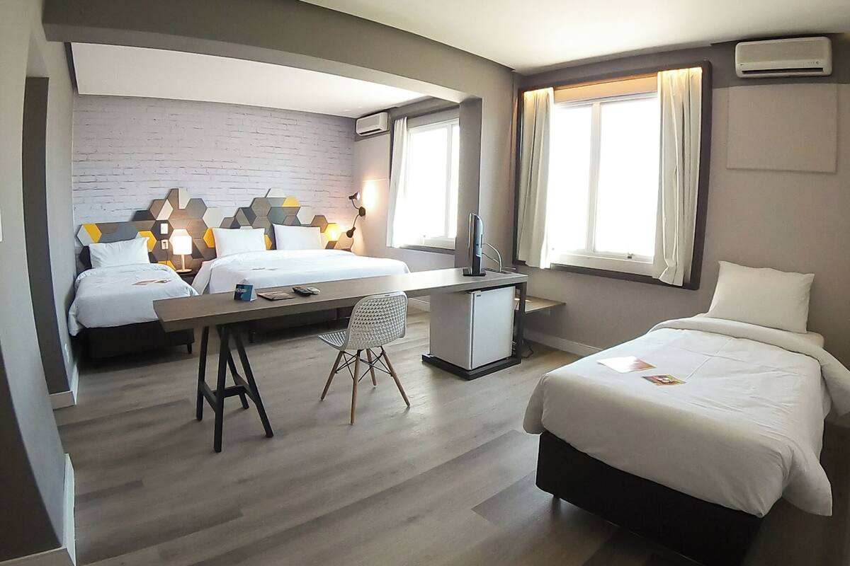Quarto de hotel moderno com duas camas, uma mesa de escritório e uma kitchenette.