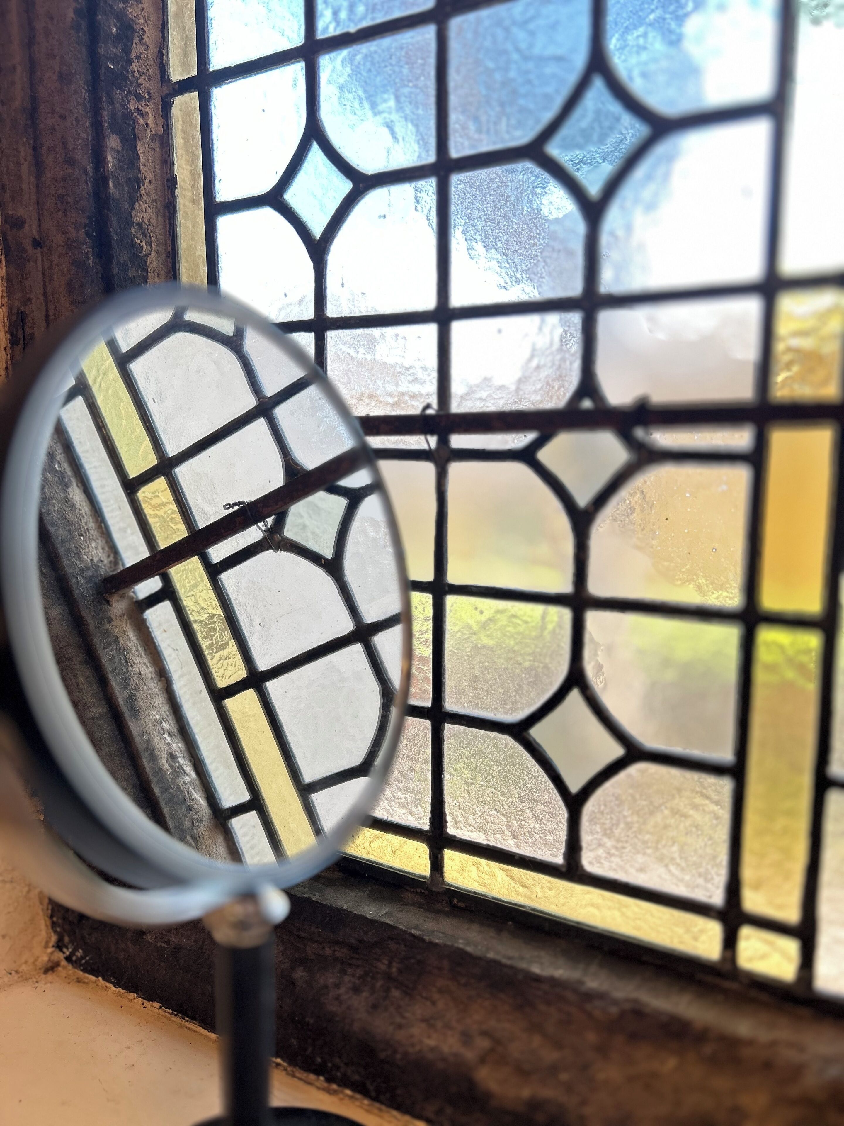 Um close-up de uma janela com uma grade decorativa e um espelho redondo refletindo parte do quarto.