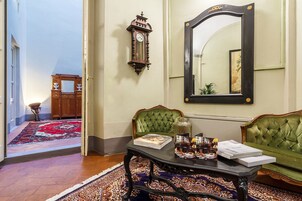 Quarto com um sofá verde, uma mesa com revistas, um relógio e um espelho na parede.