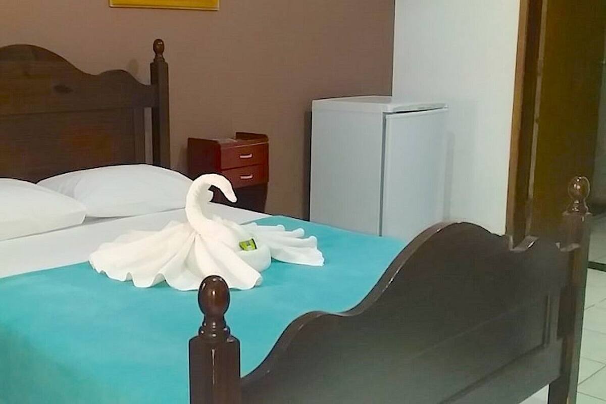 Uma cama com cabeceira de madeira, almofadas brancas, um cobreleite azul-turquesa e uma toalha dobrada em formato de cisne.