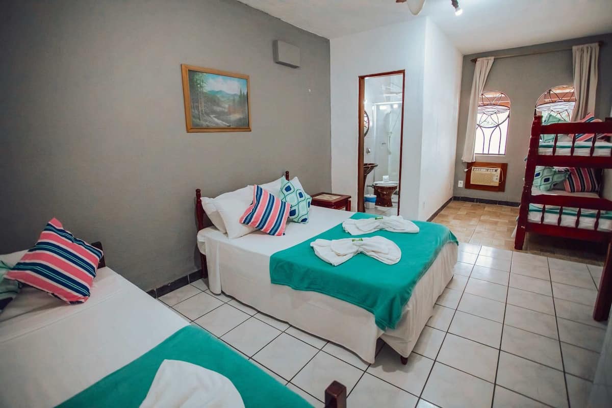 Quarto de hotel com duas camas, um quadro na parede, uma janela com cortinas e uma cadeira de madeira.