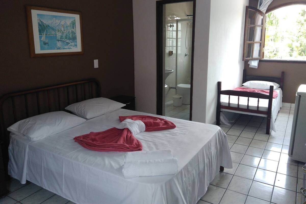 Quarto com cama, espelho, janela e um quadro na parede.
