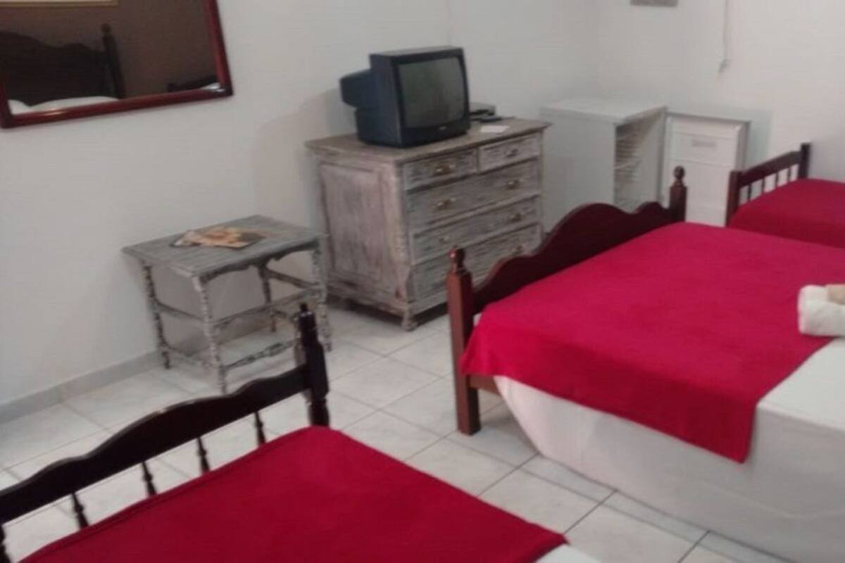 Quarto com duas camas, uma televisão em uma cômoda e uma mesinha com uma cadeira.