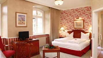 Quarto de hotel com uma cama, uma escrivaninha com um computador, uma cadeira, uma janela e um chuveiro.