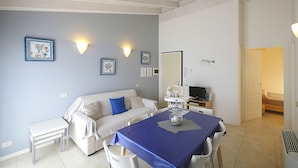 Um quarto com sofá, mesa de jantar com cadeiras, televisão e cama.