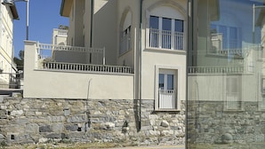 Um edifício de dois andares com base de pedra e varanda com guarda-corpo branco.