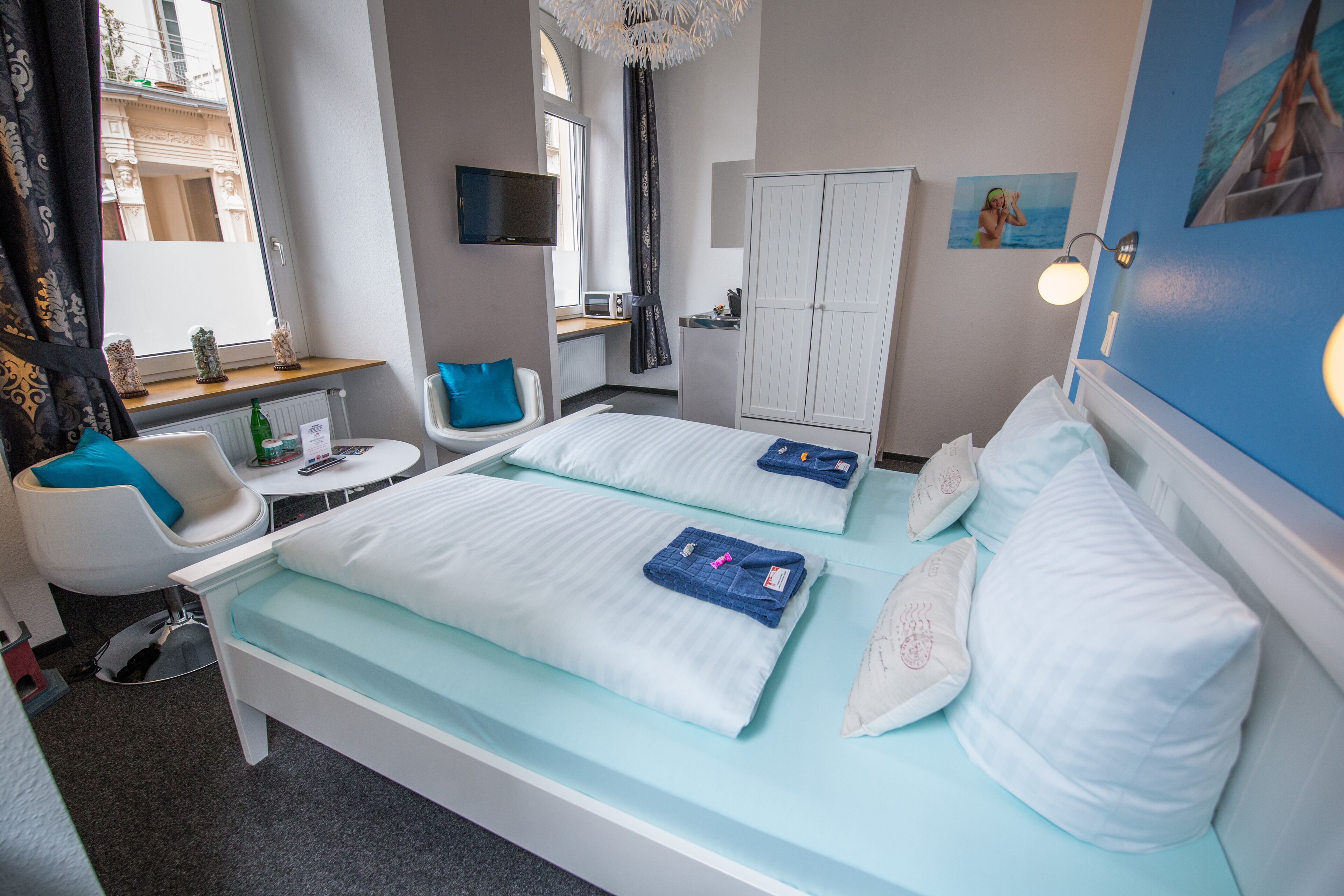 Quarto de hotel com duas camas, uma escrivaninha, uma cadeira, televisão e guarda-roupa.
