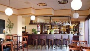 Uma área de bar com bancos e mesas de madeira, um balcão com diversos frascos e uma planta em vaso.