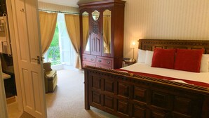 Quarto de hotel com cama de madeira, cómoda, espelho e janela com cortinas.