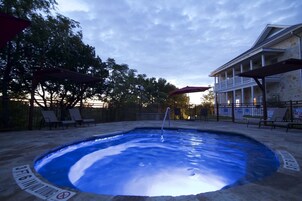 Piscina com hidromassagem, rodeada por espreguiçadeiras e guarda-sóis, com um edifício de pedra ao fundo.