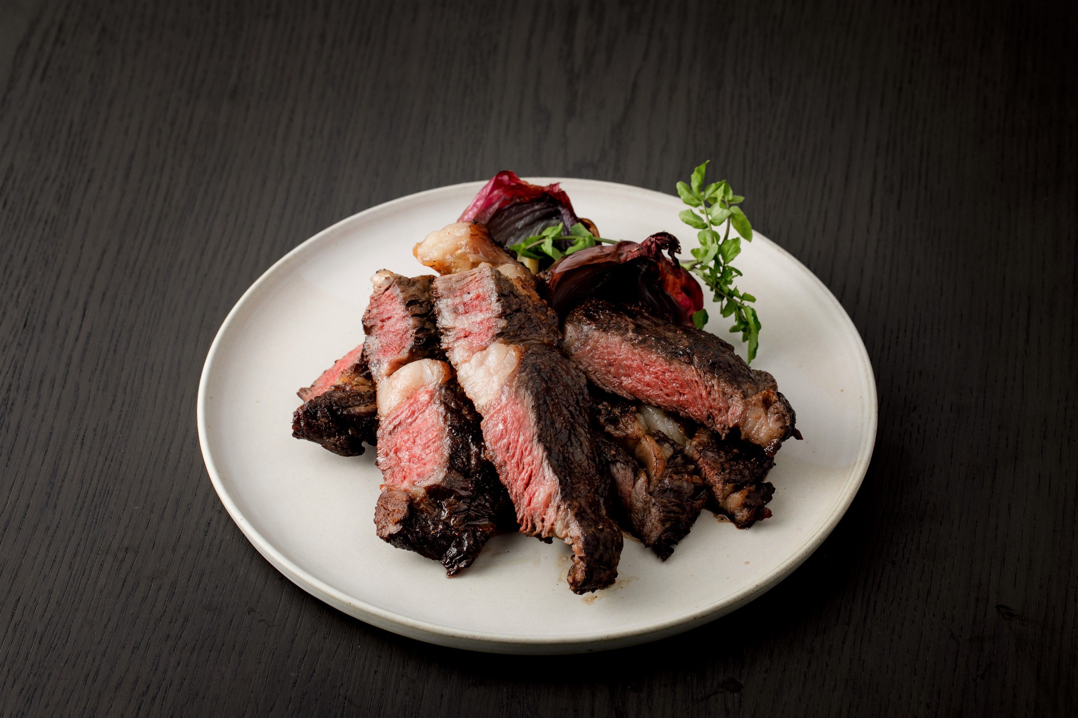 Um prato de bife fatiado com legumes sobre um fundo escuro.