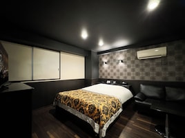 Quarto de hotel moderno com uma cama grande, uma mesa de trabalho, um sofá e ar condicionado fixado na parede.