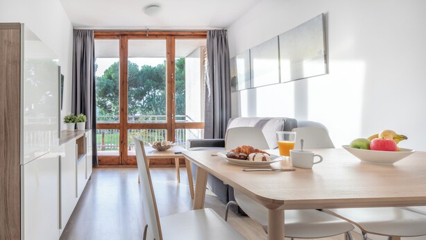 Cozinha moderna com área de refeições, uma janela grande com cortinas e uma mesa posta para o café da manhã.
