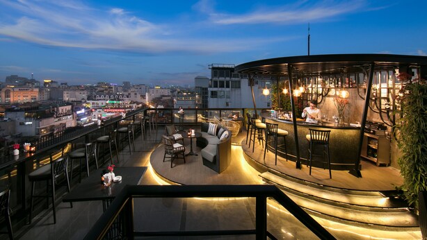 Um bar no terraço com área de estar curvada, balcão de bar e vista para o horizonte da cidade.
