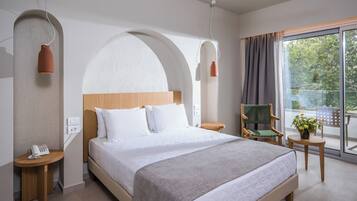 Quarto de hotel com uma cama grande, cabeceira de madeira, uma mesinha com telefone, uma cadeira e varanda com vista.