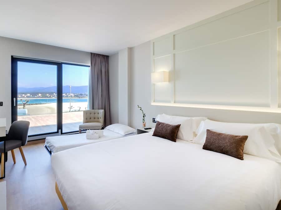 Quarto de hotel com uma cama grande, uma escrivaninha, uma cadeira e vista para a praia.