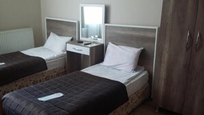 Quarto de hotel com duas camas, uma mesa de cabeceira com espelho, guarda-roupa e radiador.