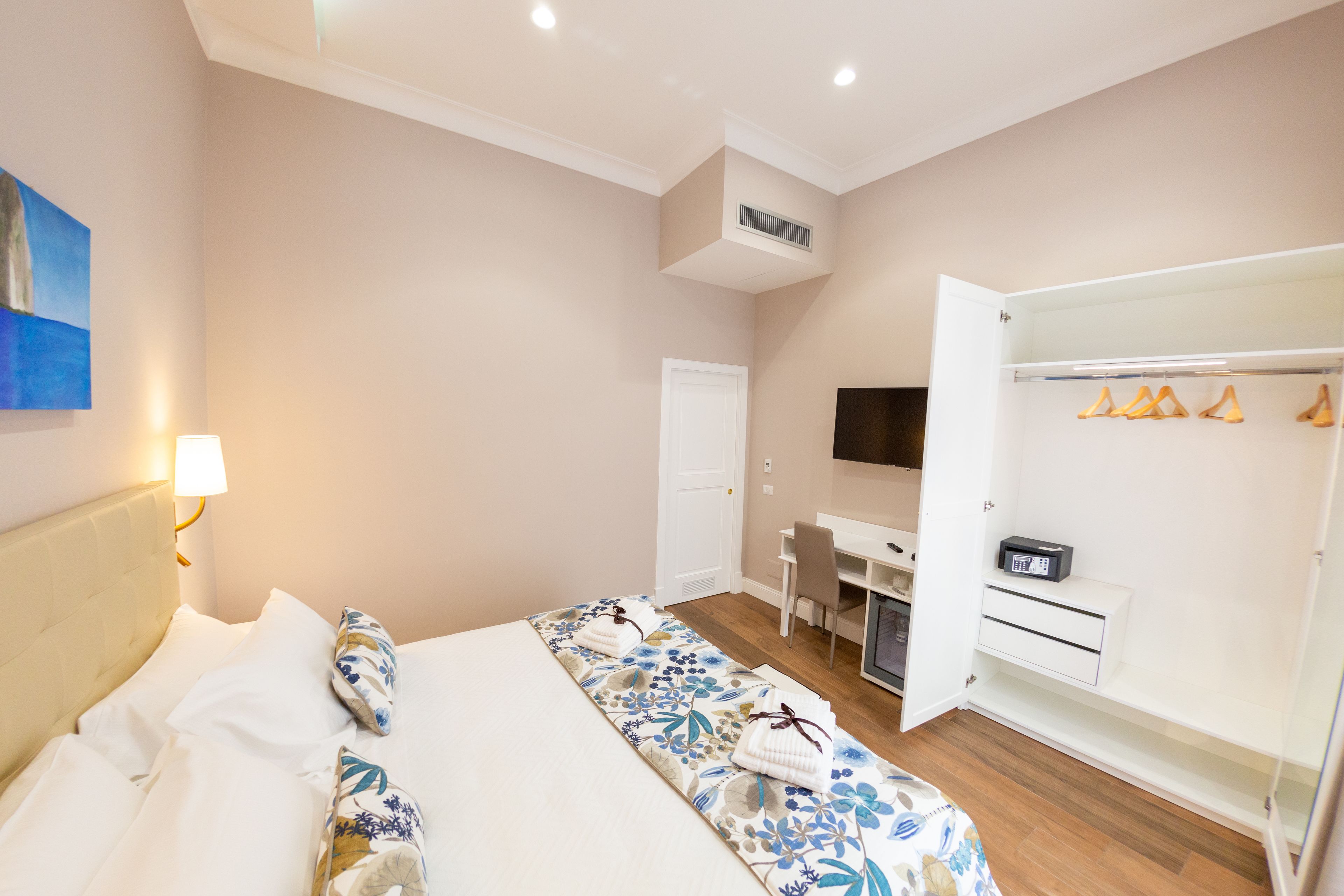 Quarto de hotel com cama, escrivaninha, guarda-roupa e televisão.