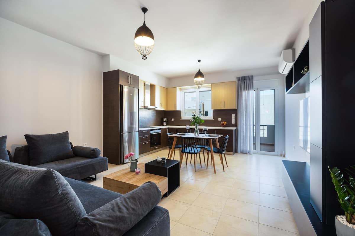 Uma sala de estar moderna com um conjunto de sofás, uma mesa de jantar e uma área de cozinha com armários e uma geladeira.