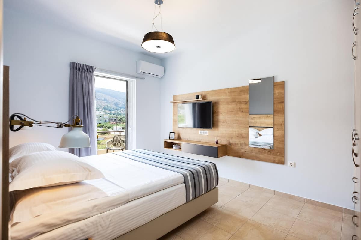 Quarto moderno com cama, televisão na parede e uma grande janela com vista para o exterior.