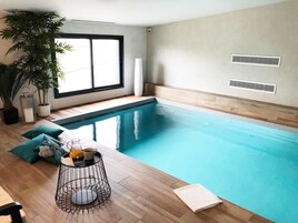 Piscina interna com piso de madeira, uma mesa com uma bebida e um vaso de planta.