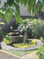 Um jardim com uma fonte de pedra, nenúfares e plantas floridas.